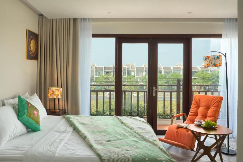 Quarto de hotel com cama, cadeira, mesa e varanda com vista para prédios.