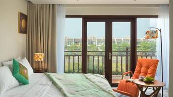 Quarto de hotel com cama, cadeira, mesa e varanda com vista para prédios.