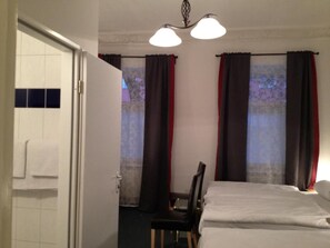 Quarto de hotel com cama, cadeira e escrivaninha.