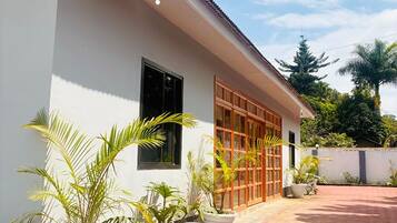 Um edifício branco com telhado de cerâmica, garagem com portas de vidro e plantas em vasos ao longo da passarela.