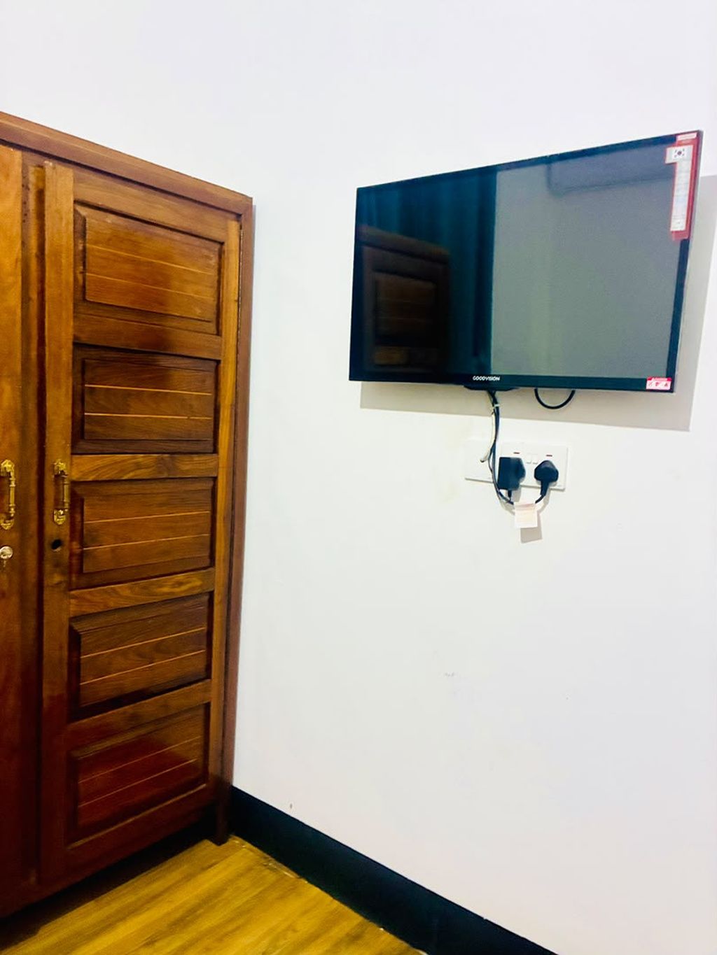 Uma porta de madeira e uma televisão fixada numa parede branca.
