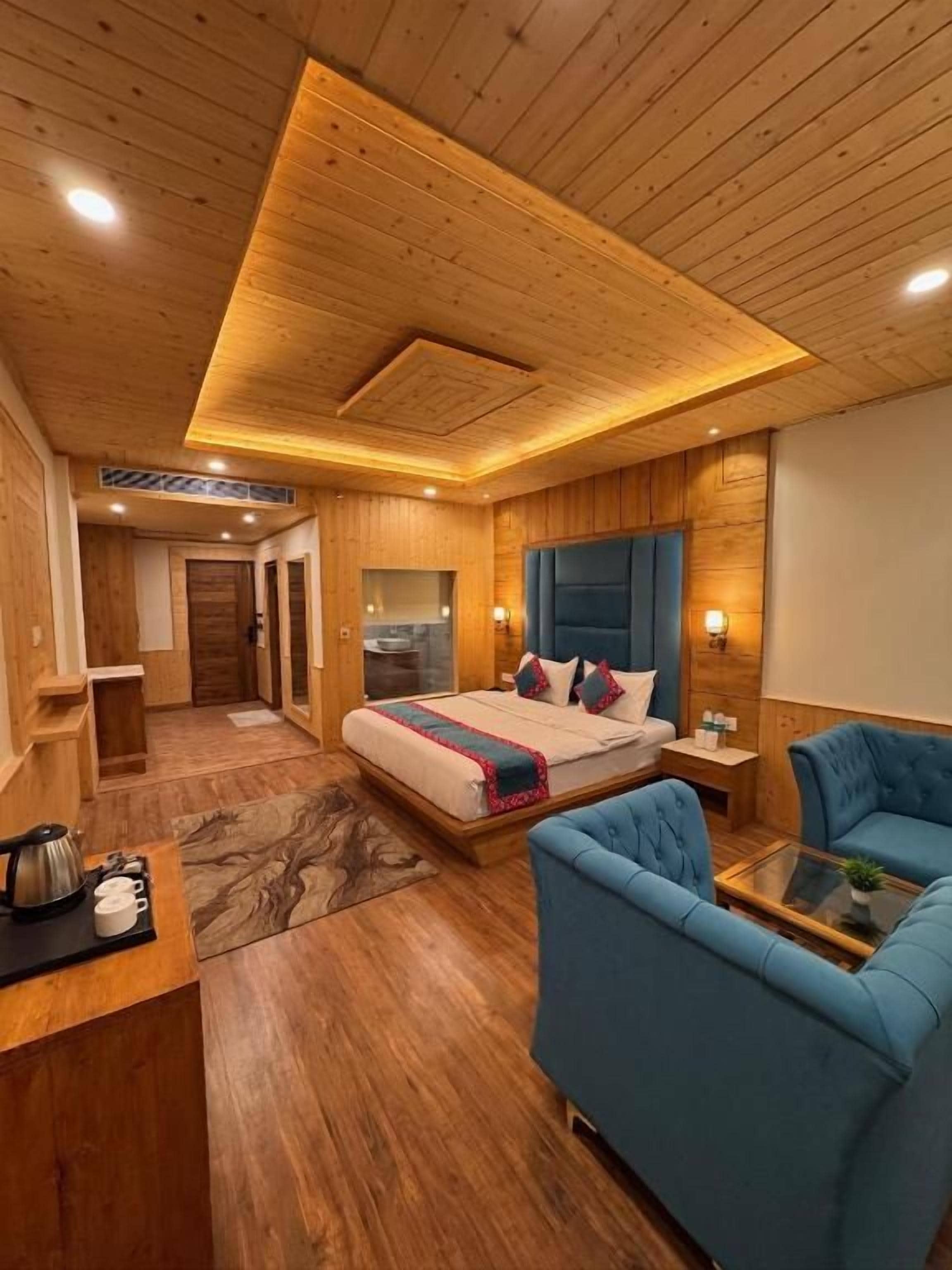 Quarto de hotel com teto de madeira, cama com almofadas, poltrona azul, mesa pequena e mesa de cabeceira.