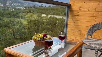 Uma varanda com mesa de vidro, cadeiras de vime e vista para uma paisagem montanhosa.