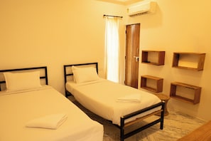 Quarto de hotel com duas camas, porta de madeira, aparelho de ar condicionado e prateleiras de madeira.