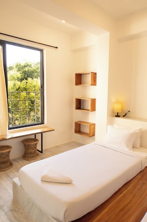 Quarto com cama grande, janela com vista para o verde e prateleiras de madeira embutidas.