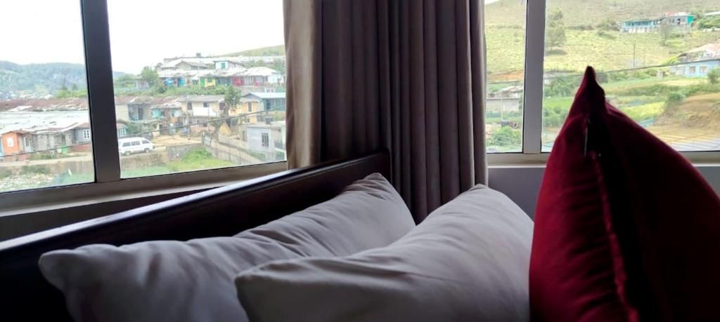 Uma cama com roupa de cama branca e um travesseiro vermelho, uma janela com cortinas e vista para uma área residencial.