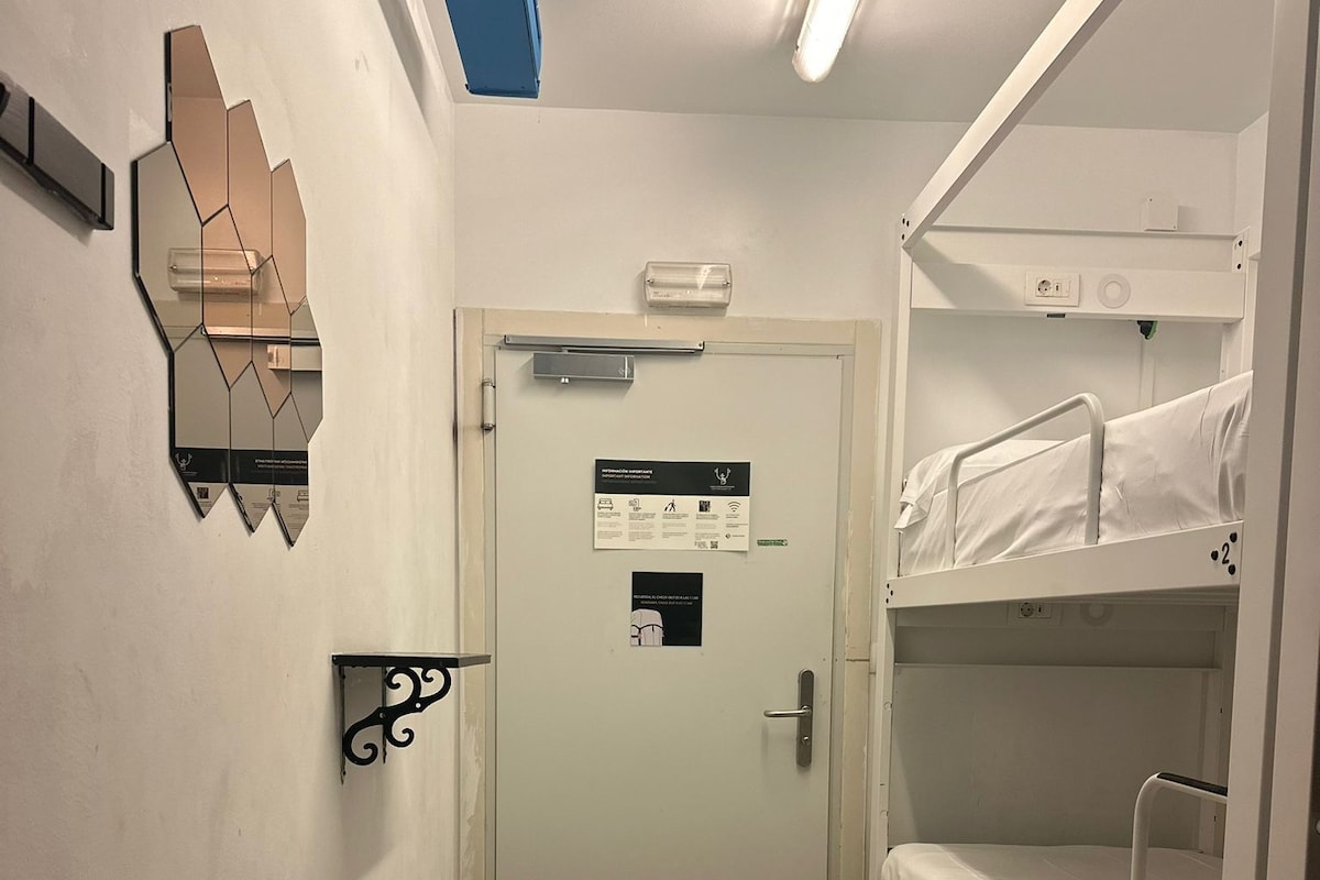 Um corredor estreito com uma porta, um espelho e uma cama beliche com colchão e travesseiro.