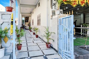 Corredor com plantas em vasos, um portão azul e piso de azulejos.