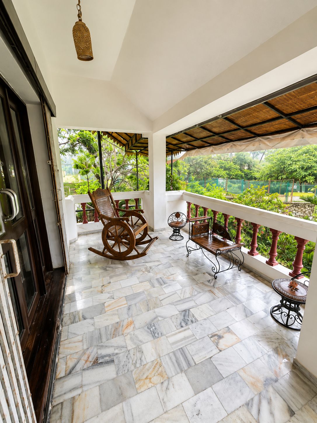 Varanda com vista para um jardim exuberante, uma cadeira de balanço e uma mesa com cadeiras.