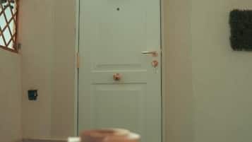 Uma porta branca com uma placa em cima, um banquinho de madeira na frente e um tapete verde no chão.