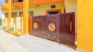 Um edifício com fachada amarela, entrada protegida por grades e um logotipo, e escadaria que leva à entrada.
