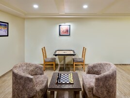 Quarto com um tabuleiro de xadrez sobre uma mesa, duas cadeiras e um quadro na parede.