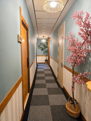 Corredor de hotel com carpete xadrez, portas de madeira e uma cerejeira.
