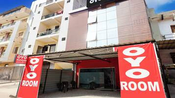 Um hotel chamado OYO, com toldo vermelho e placas, um edifício de vários andares com varandas, e um céu azul claro.