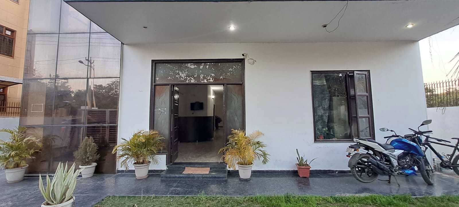 Entrada de um edifício moderno com porta de vidro, plantas em vasos e uma moto estacionada.