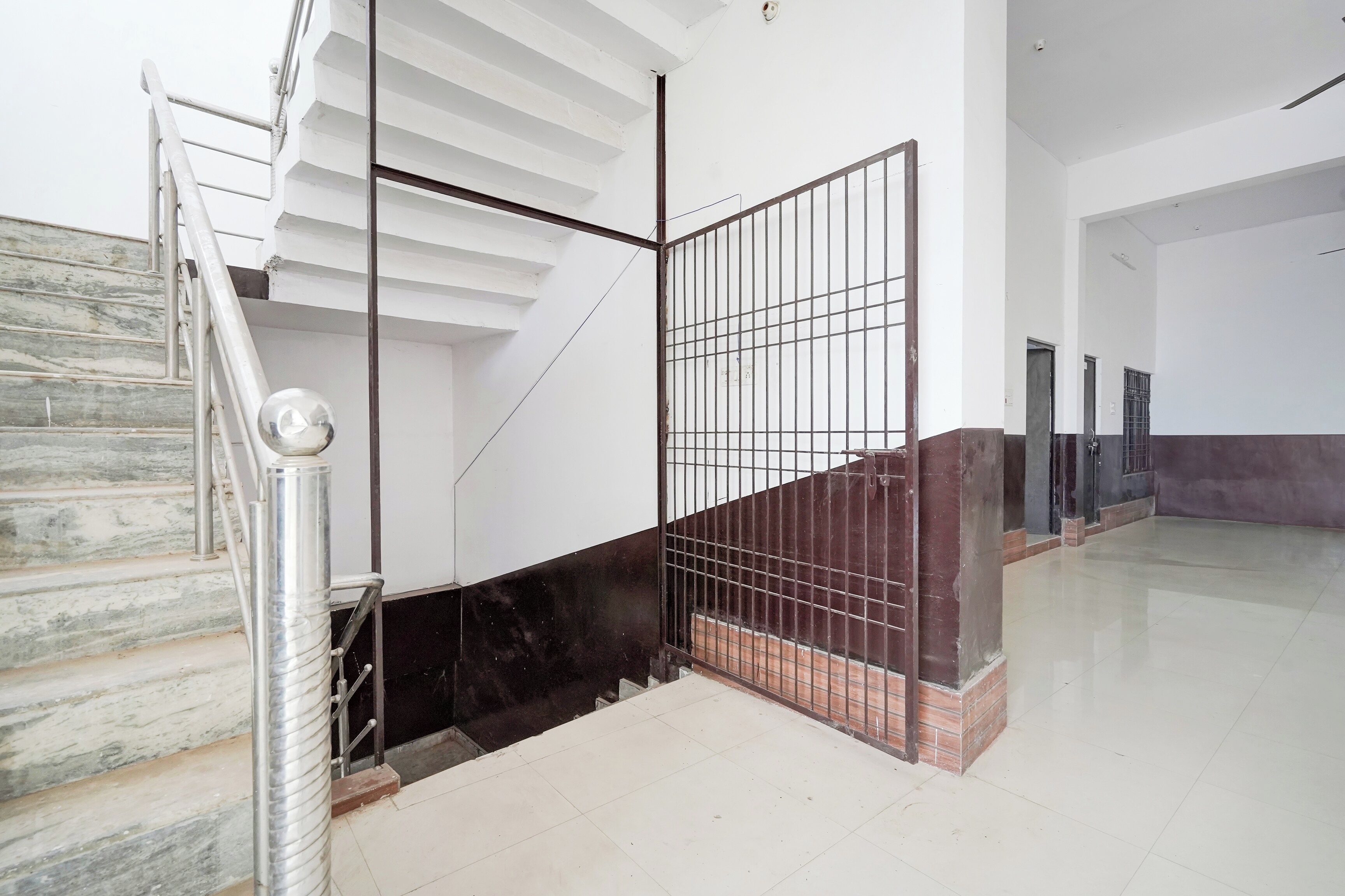 Escadaria com guarda-corrimão de metal, portão preto e parede de mármore.