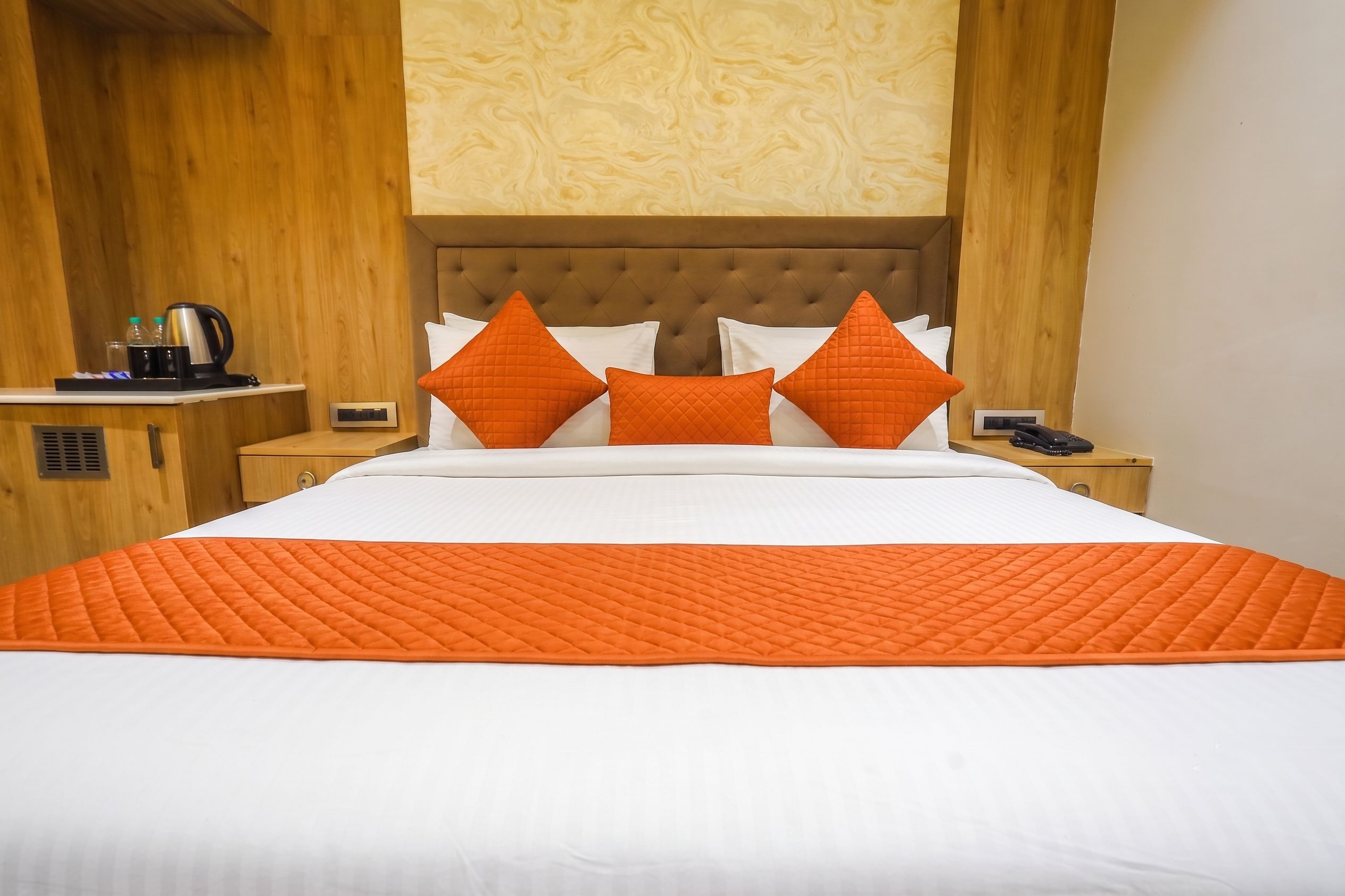 Quarto de hotel com uma cama grande, cabeceira de madeira e mesa de cabeceira com telefone e chaleira.