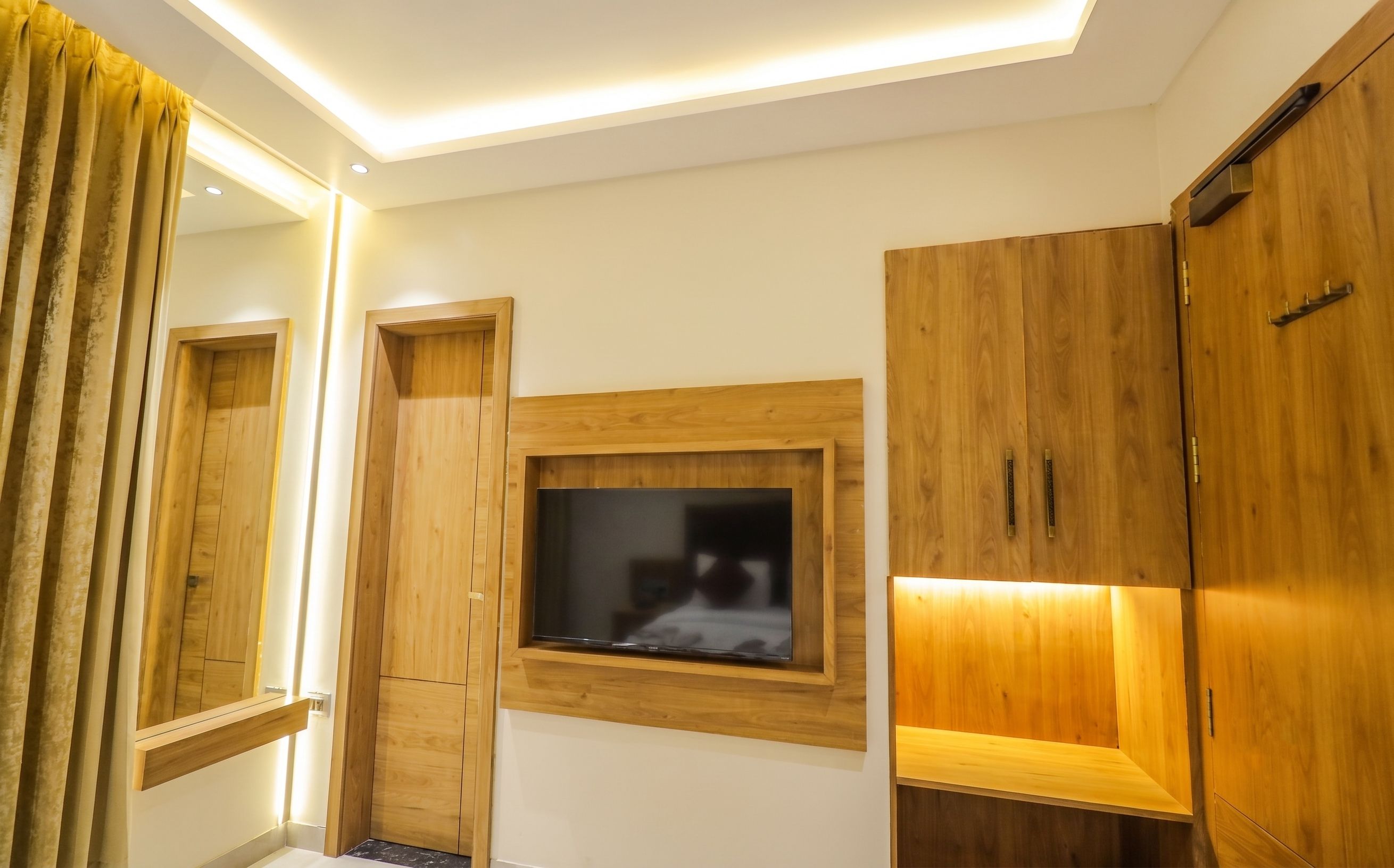 Quarto com armários de madeira, televisão fixada na parede e espelho.