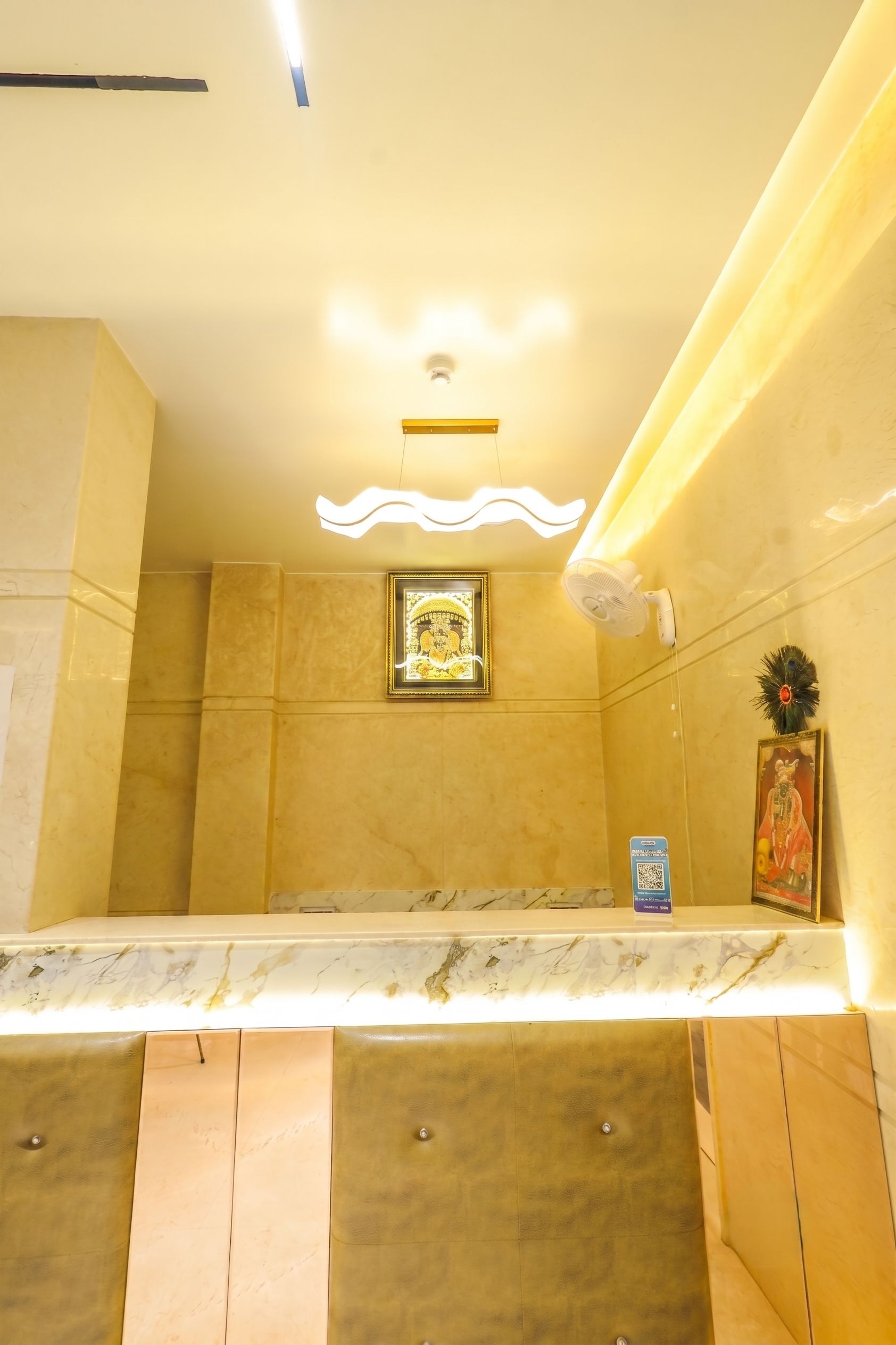 Uma área de recepção de hotel com balcão de mármore, uma peça religiosa emoldurada na parede e um lustre no teto.