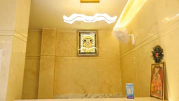 Uma área de recepção de hotel com balcão de mármore, uma peça religiosa emoldurada na parede e um lustre no teto.