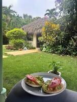 Um jardim com uma construção de colmo, gramado e uma mesa com comida.