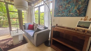 Uma sala de estar aconchegante com um sofá, uma mesinha, uma luminária, um quadro e um aparador de madeira.