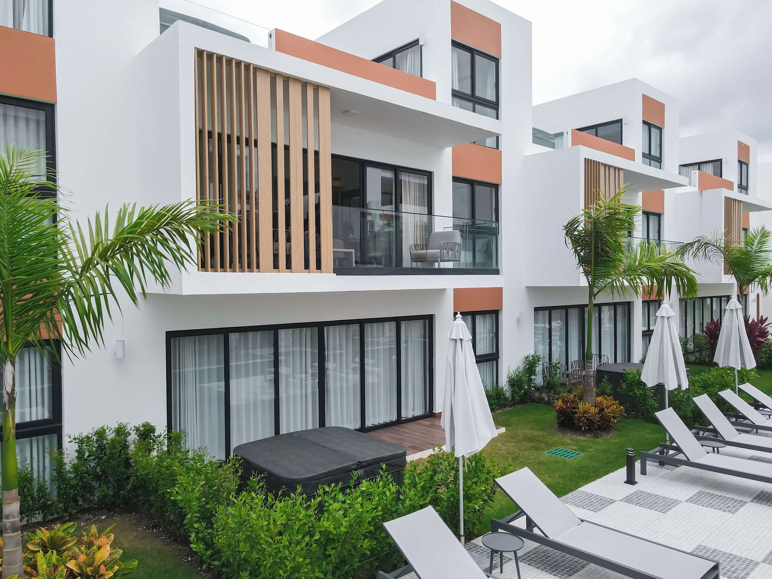 Um hotel moderno de vários andares, com varandas, área de estar ao ar livre e vegetação exuberante.
