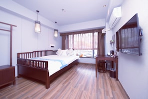 Quarto de hotel com cama de madeira, escrivaninha, cadeira, janela com cortinas e ar condicionado.