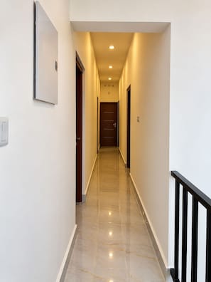 Corredor com piso de mármore, paredes brancas e corrimão preto.