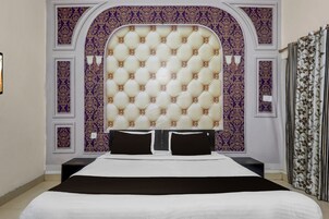 Quarto com cabeceira estofada, cama com roupa de cama branca e parede com padrão floral.