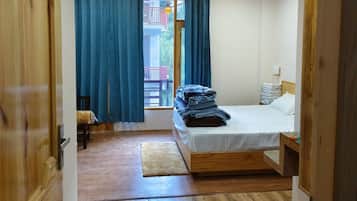 Quarto com cama, janela com cortinas, piso de madeira e tapete estampado.