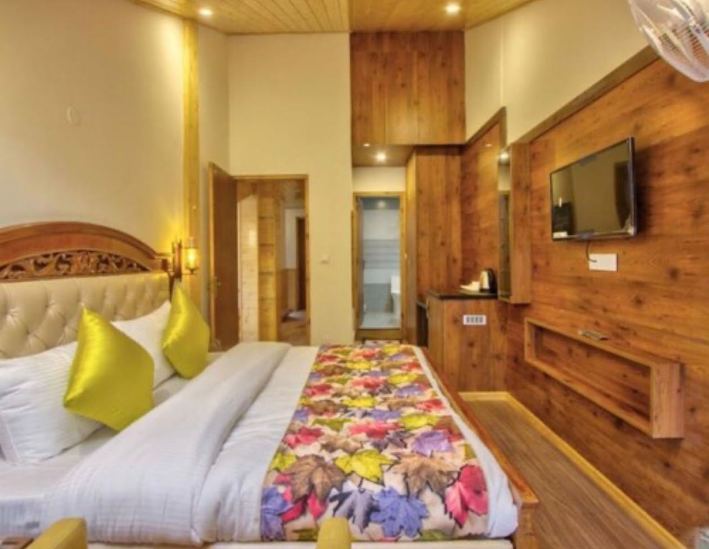 Quarto com cama, televisão fixada na parede e cabeceira de madeira.