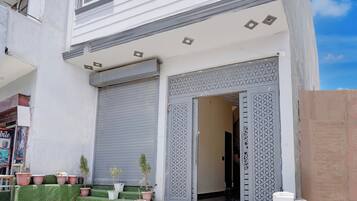 Um edifício com uma porta de obturador fechada, um portão de metal decorativo e plantas em vasos nos degraus.