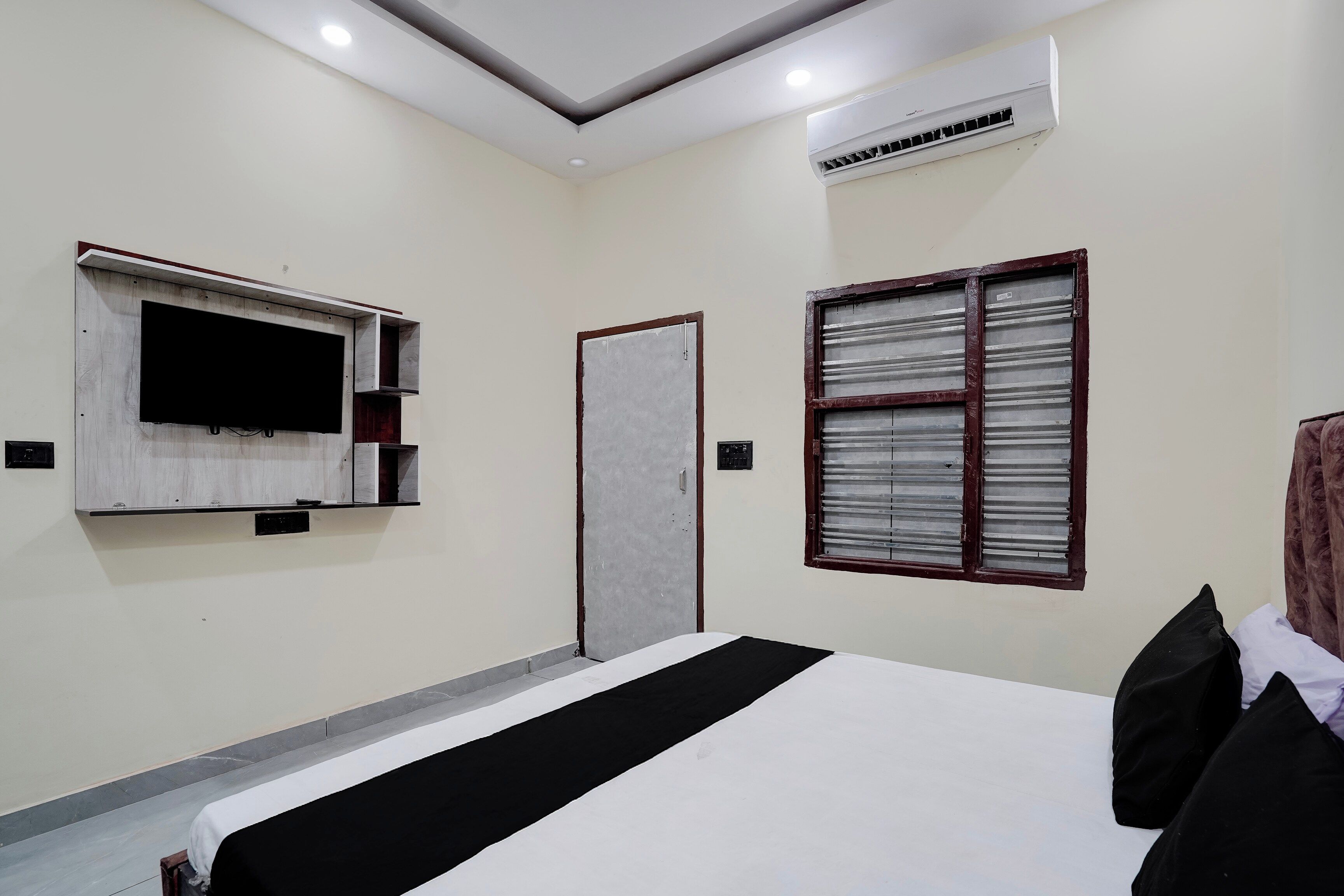 Quarto de hotel com cama, televisão de tela plana na parede, ar condicionado e janela com persianas.