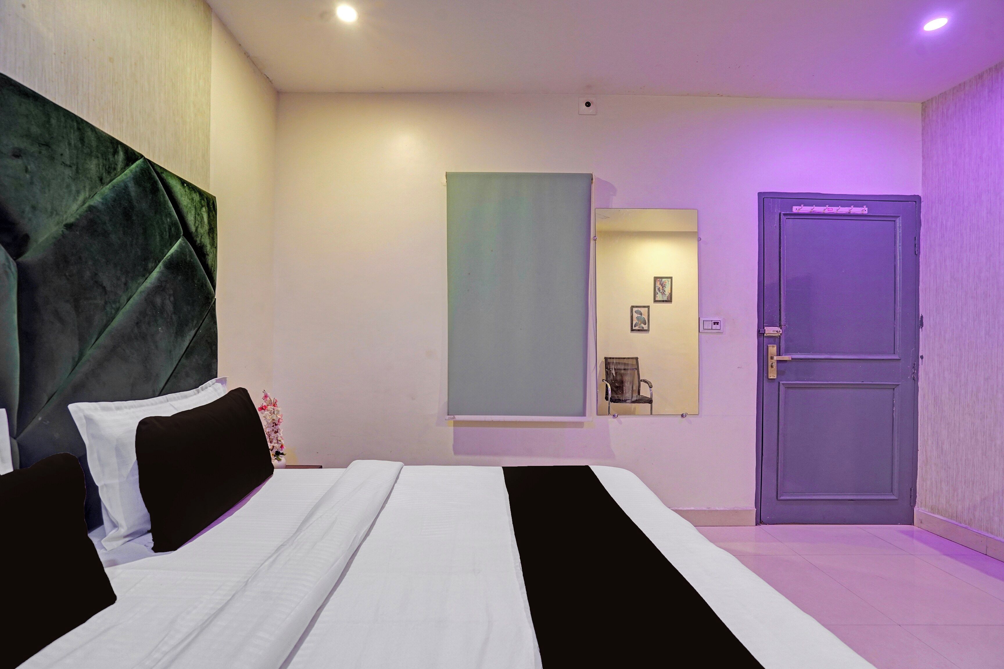 Quarto de hotel com cama, porta, espelho e uma obra de arte pendurada na parede.