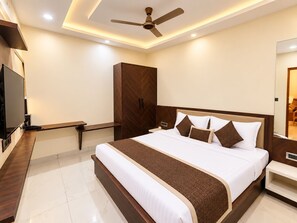 Quarto de hotel com cama grande, armário, televisão e ventoinha no teto.