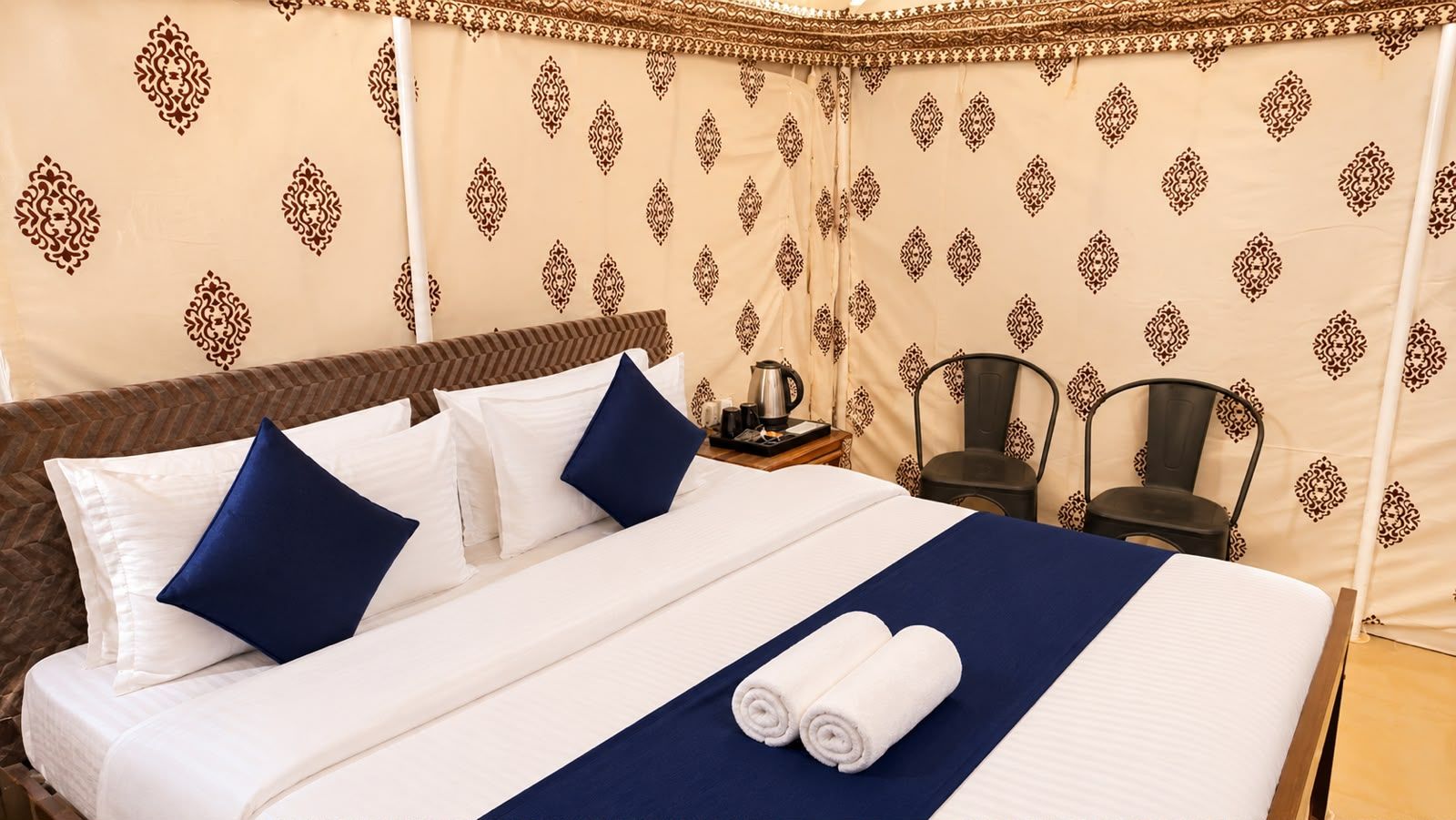 Quarto de hotel com cama, almofadas, mesa de cabeceira, cadeira e cortina com padrão.