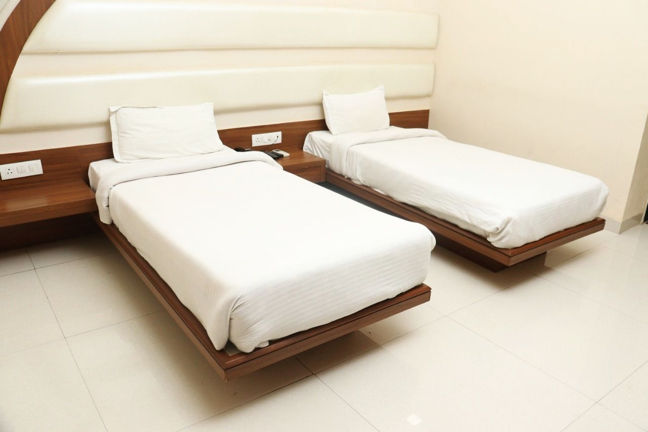 Duas camas de solteiro com estrutura de madeira e roupa de cama branca em um quarto de hotel.