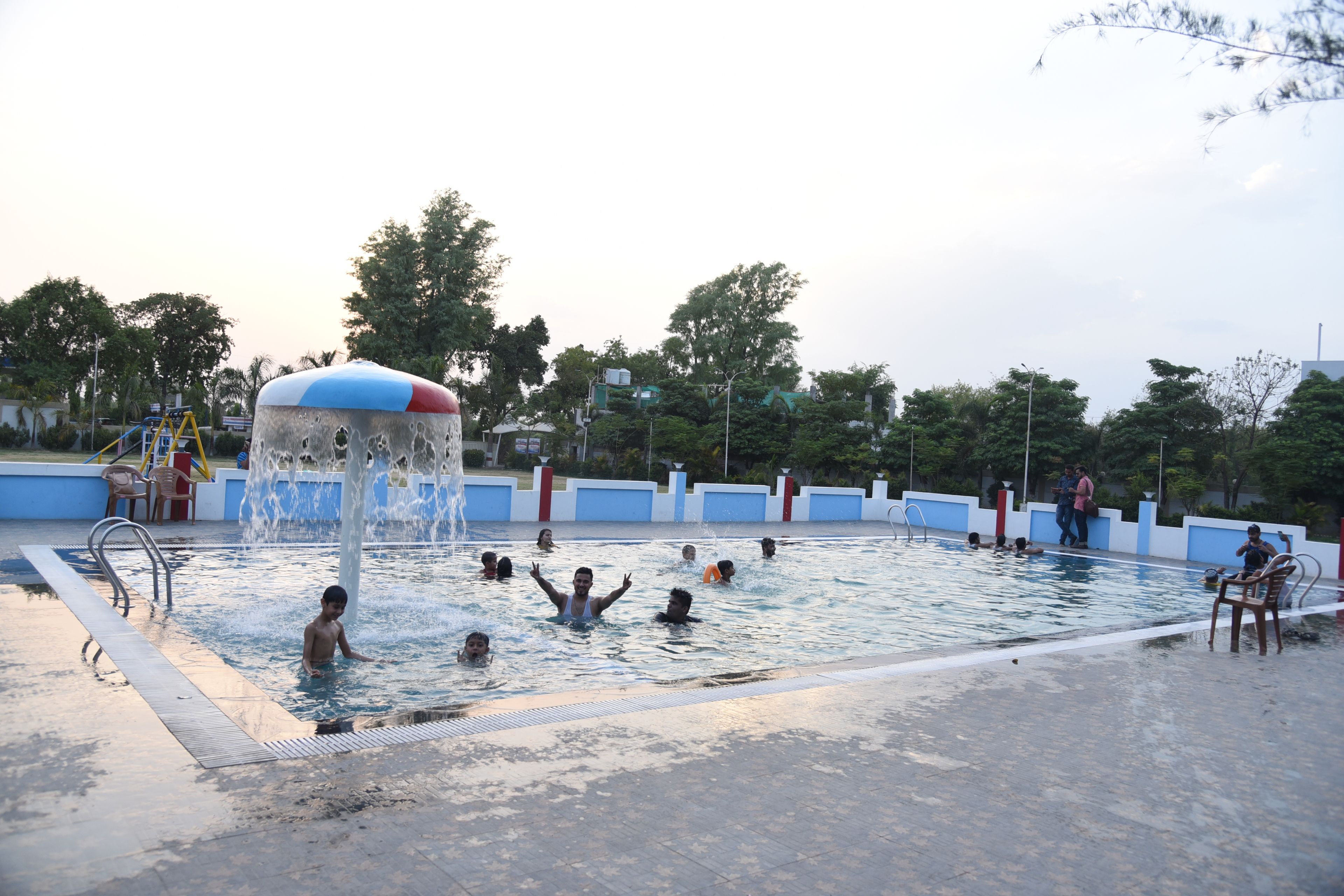 Piscina com fonte, cercada por um muro baixo e árvores.