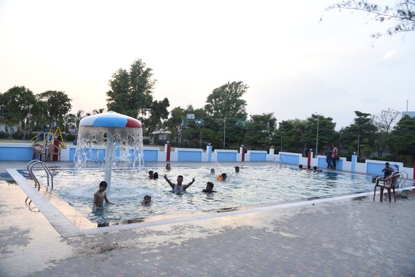 Piscina com fonte, cercada por um muro baixo e árvores.