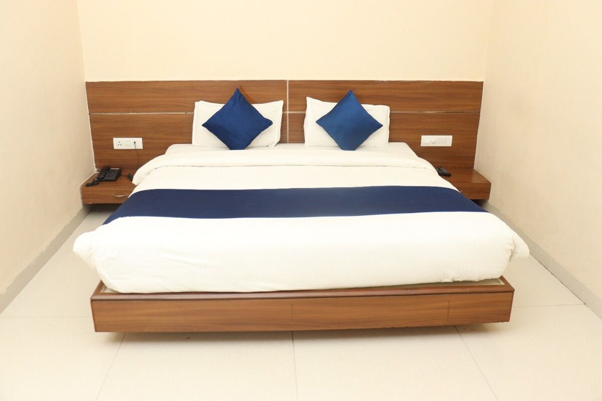 Uma cama com cabeceira de madeira, dois travesseiros, um cobre-leito branco e azul, e uma mesa de cabeceira com um telefone.
