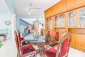 Uma sala de jantar com uma mesa de vidro redonda, cadeiras estofadas vermelhas e um armário de madeira com portas de vidro.
