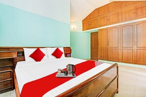 Quarto de hotel com cama, guarda-roupa de madeira e mesa de cabeceira.
