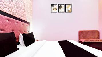 Quarto de hotel com uma cama grande, cabeceira, área de estar e três obras de arte penduradas na parede.