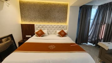 Quarto de hotel com uma cama grande, cabeceira com uma parede texturizada ao fundo e vista para o exterior através de uma janela com cortinas.