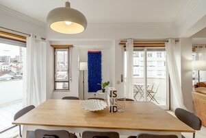 Uma sala de jantar moderna com uma mesa de madeira, cadeiras, um lustre e vista para a cidade através de grandes janelas.