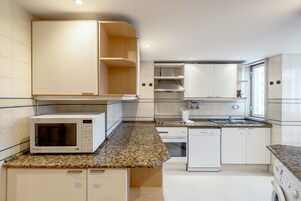 Uma cozinha moderna com armários brancos, micro-ondas embutido, lava-louças Bosch e bancadas de granito.