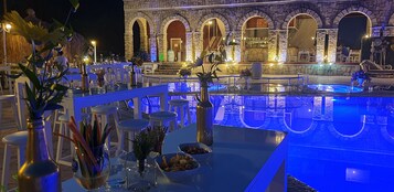 Área de piscina externa com arcos de pedra, assentos de bar e mesas com guarda-sóis.