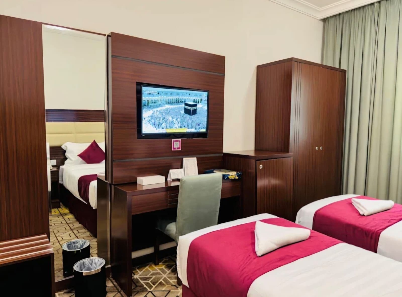 Quarto de hotel com cama, escrivaninha, televisão e guarda-roupa.