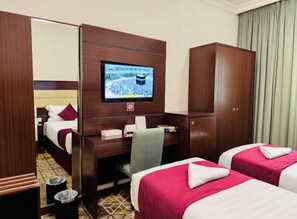 Quarto de hotel com cama, escrivaninha, televisão e guarda-roupa.